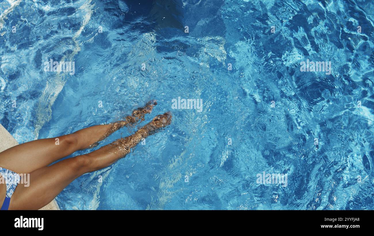 Woman is sitting at the edge of the pool with her legs dangling in the ...