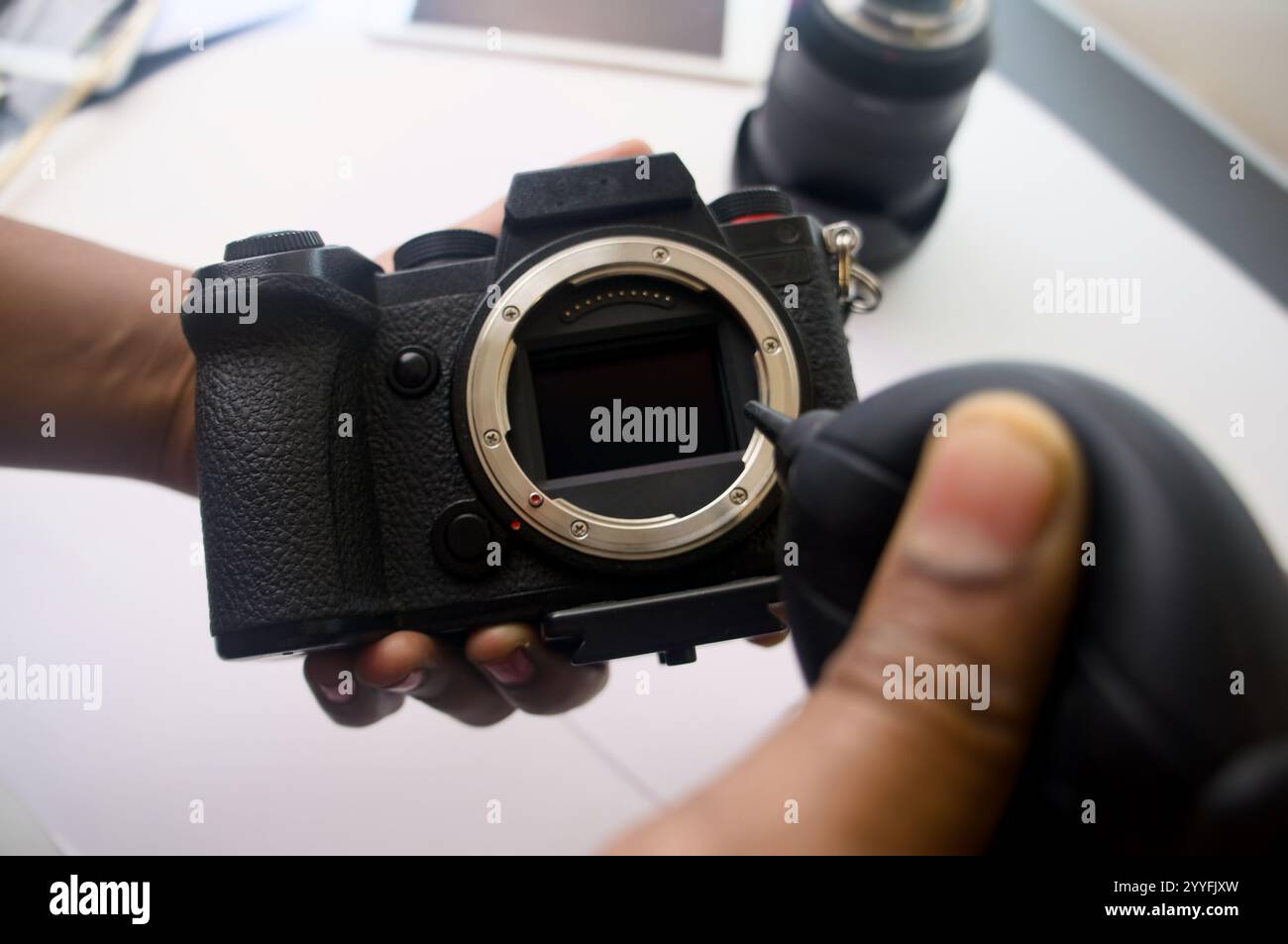 Hands cleaning a mirrorless camera sensor with a blower. Maintaining ...