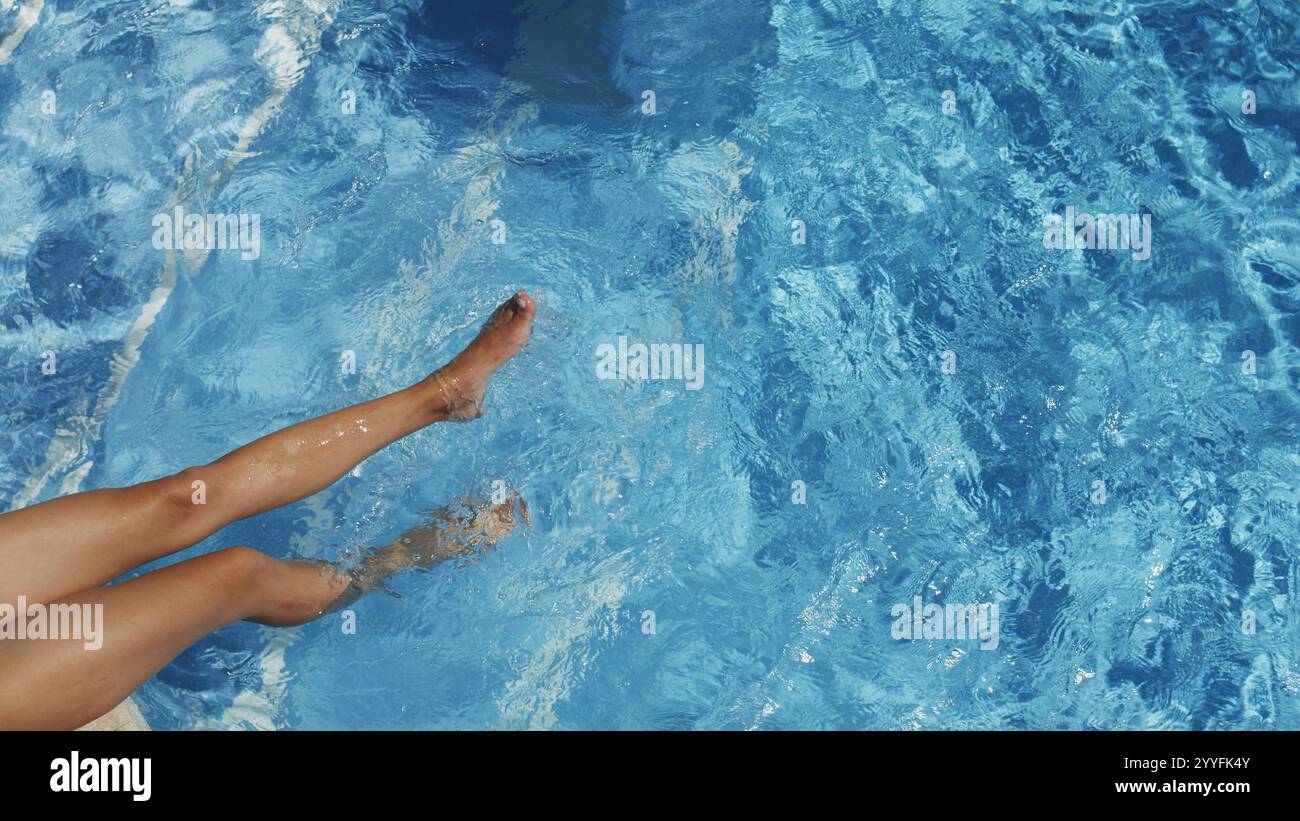 Woman is sitting at the edge of the pool with her legs dangling in the ...