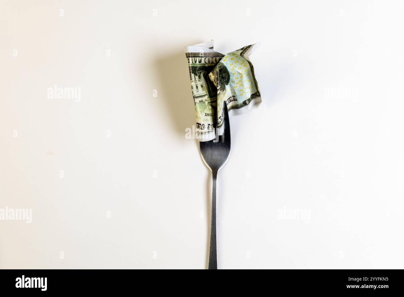 Crumpled hundred dollar bill speared on a fork against a white ...