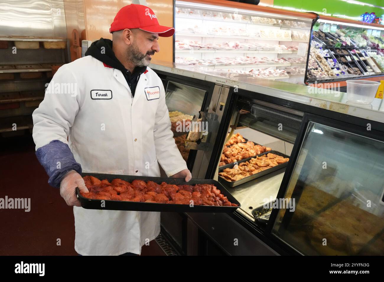 Marinated chicken is put out onto the display counter at an Adonis ...