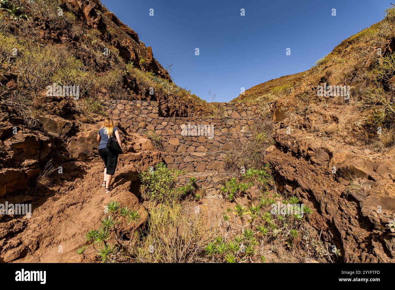 A person is walking down a rocky path with a backpack. The path is ...
