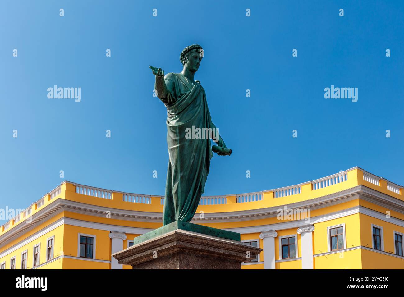 A statue of a man stands in front of a yellow building. The statue is ...