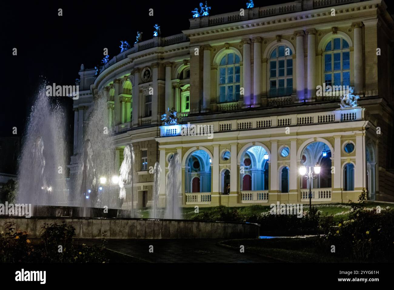A large building with a fountain in front of it. The fountain is lit up ...