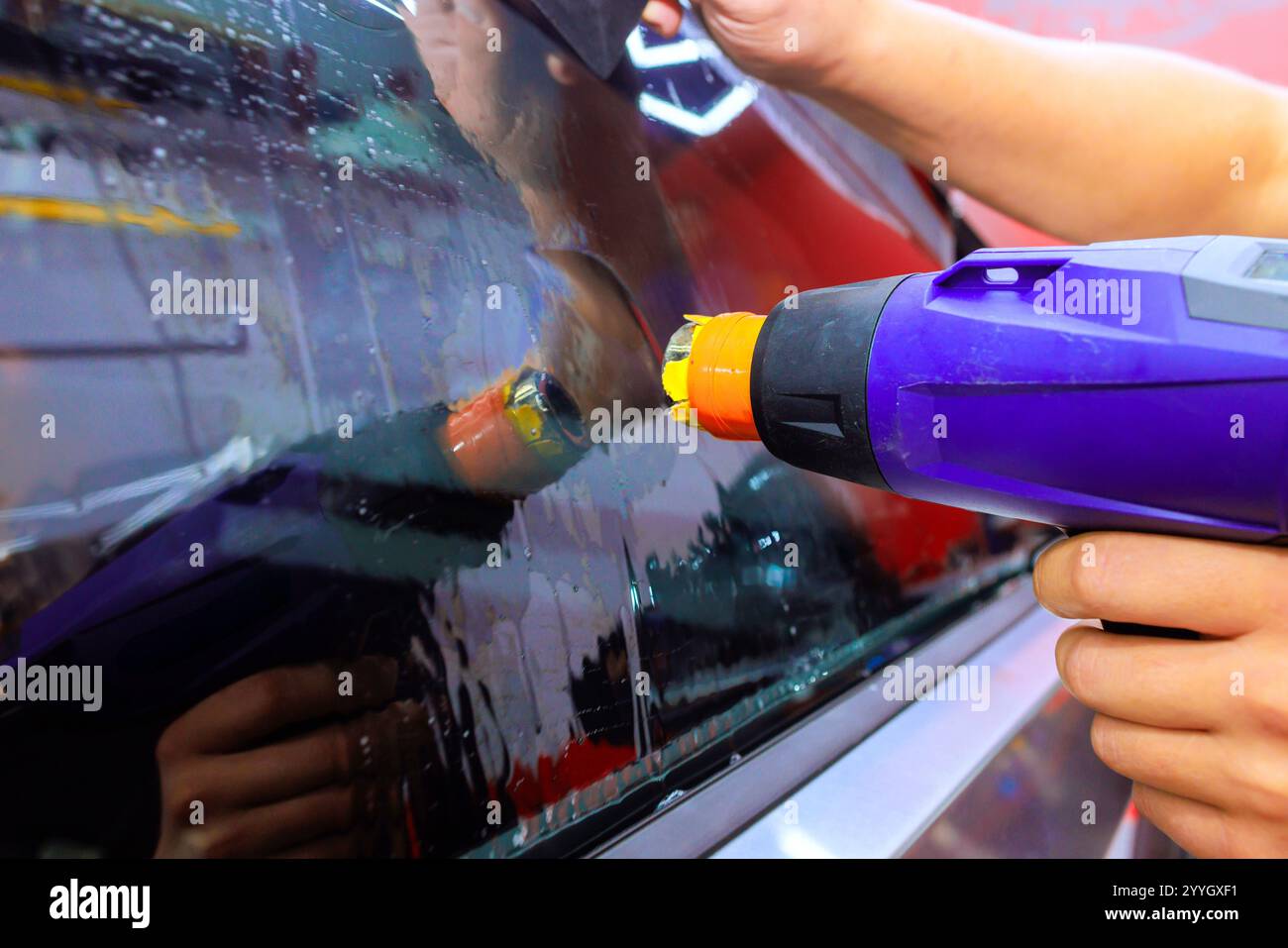 Technician worker uses heat gun to carefully strip window film from car ...