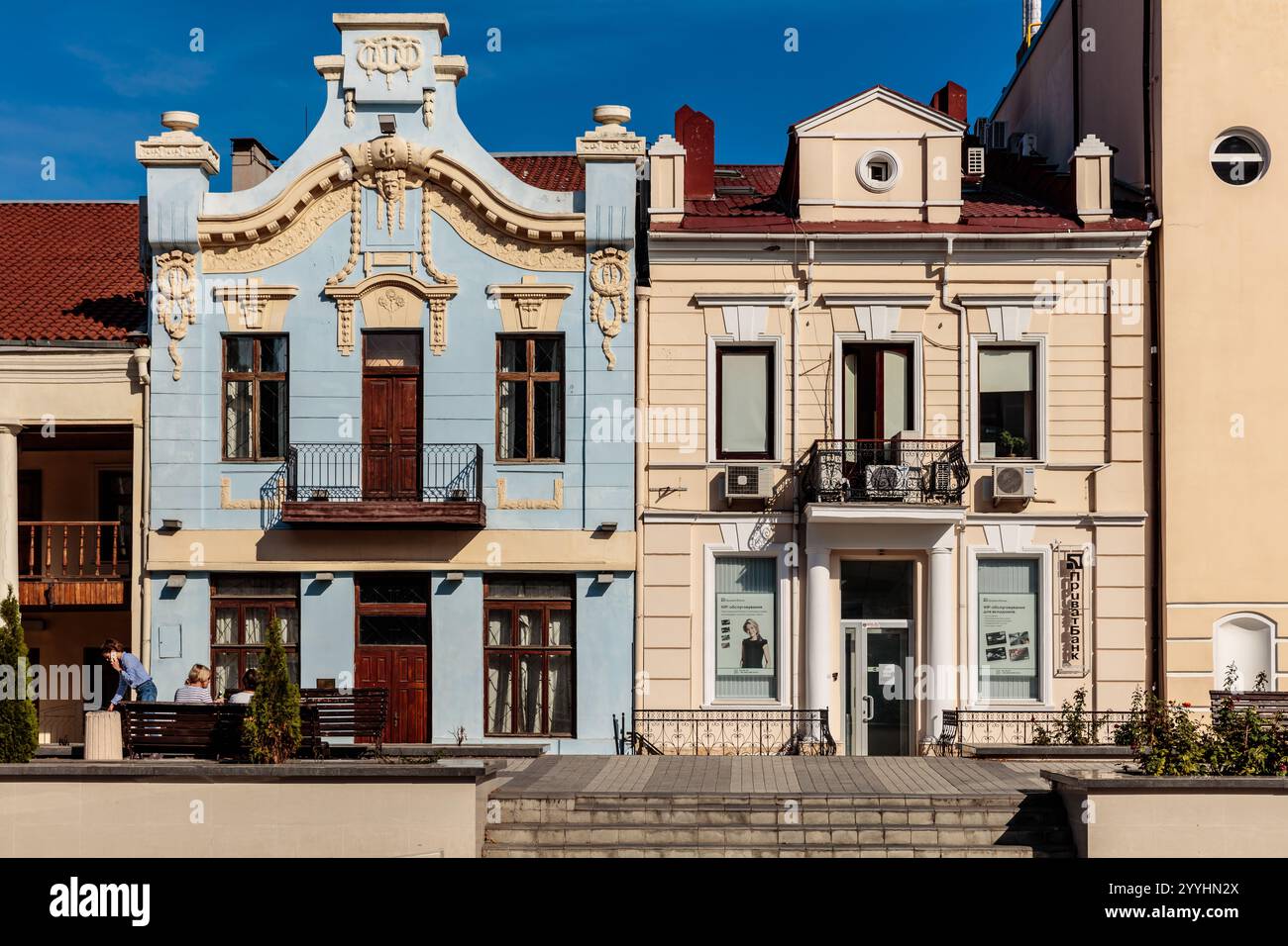 Two old buildings with a balcony and a bench in front of them. The ...
