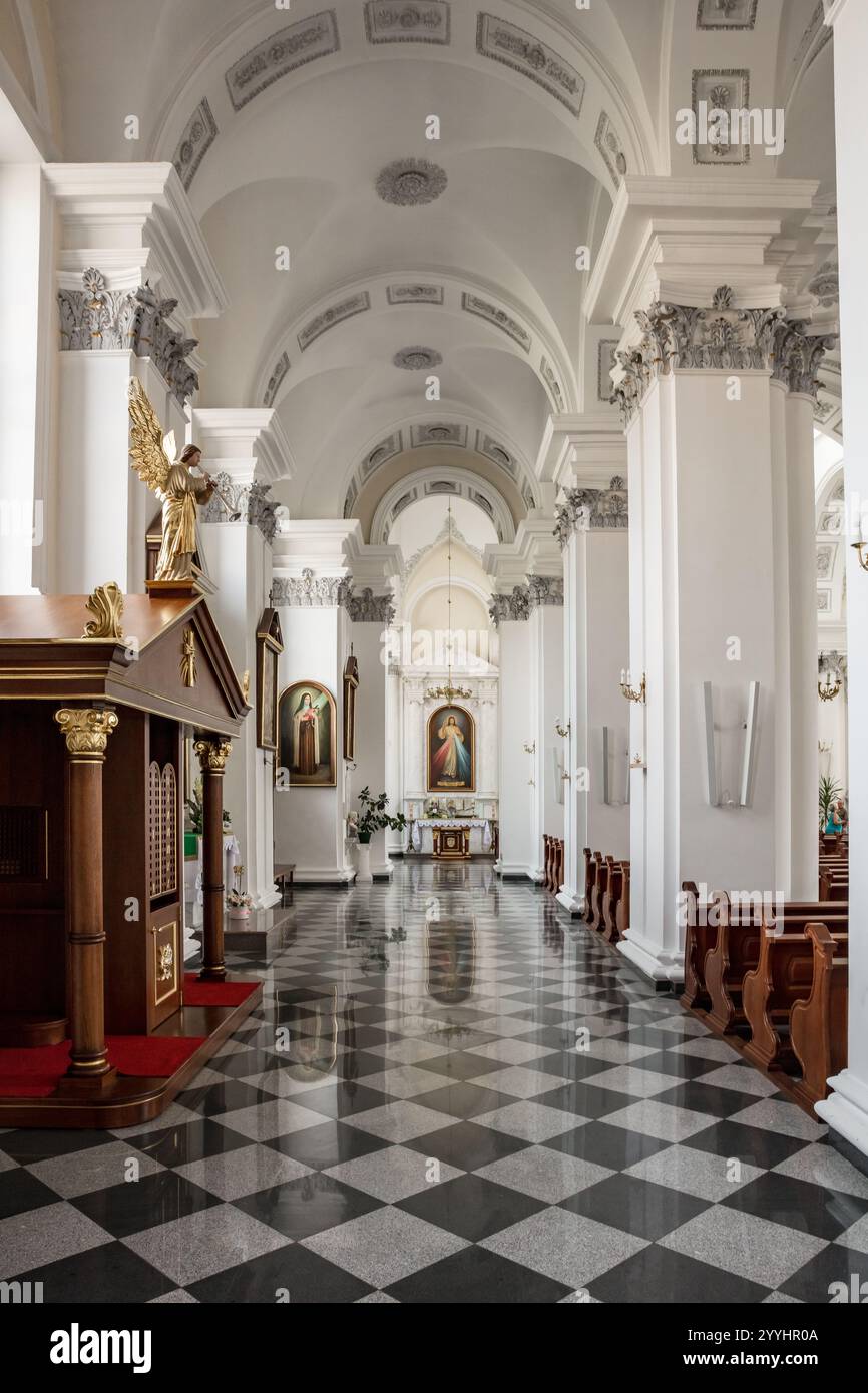 A long, narrow room with white pillars and a wooden altar. The room is ...