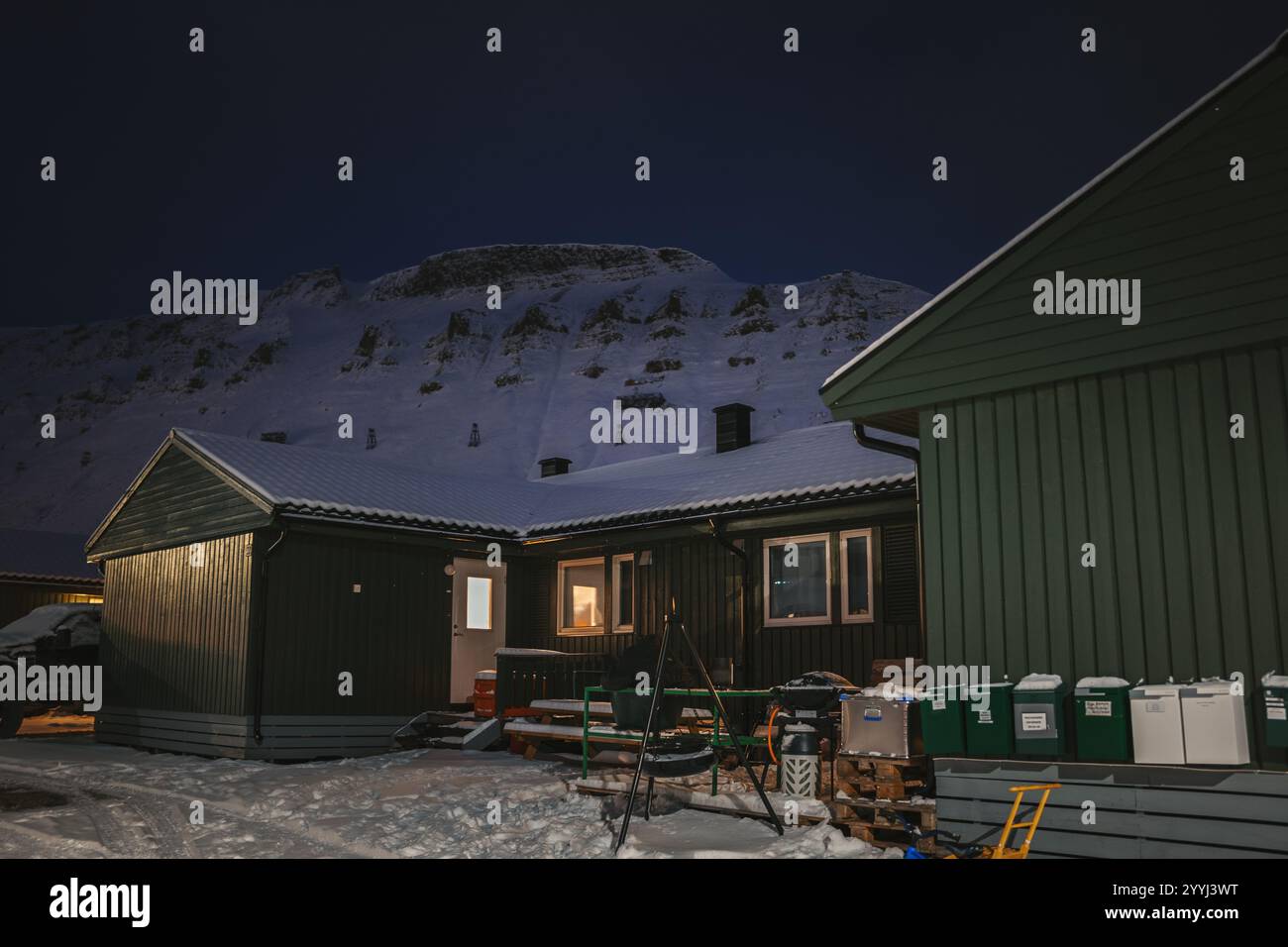 Wooden house under snowy mountains in the polar night in Longyearbyen ...