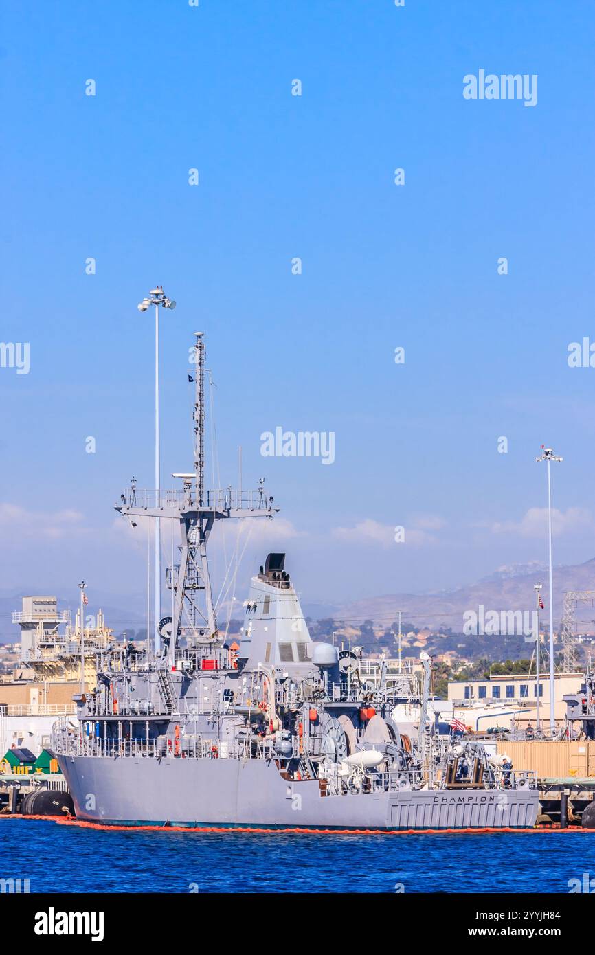 A large navy ship is docked at a pier. The sky is clear and blue, and ...