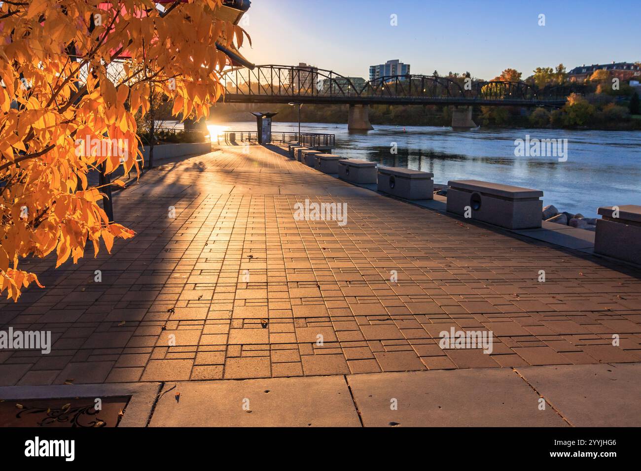 A bridge spans a river with a brick walkway on the other side. The ...
