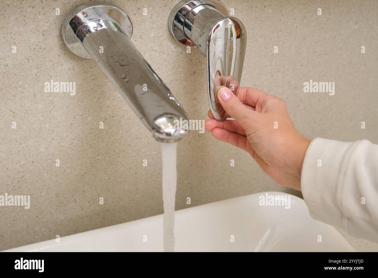 Hand adjusting faucet handle with water running in modern bathroom sink ...