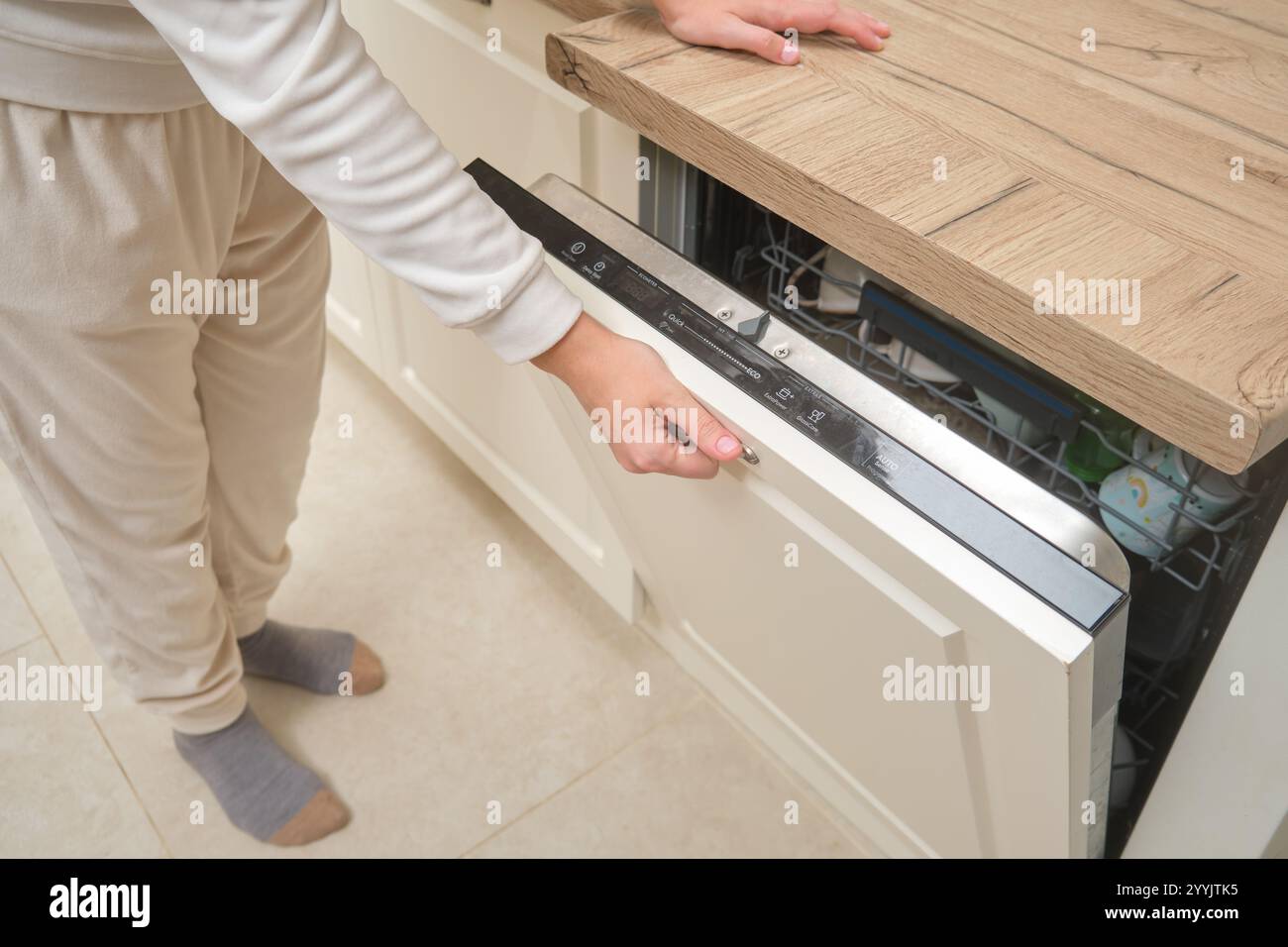 Person opening dishwasher in a modern kitchen with wooden countertop ...