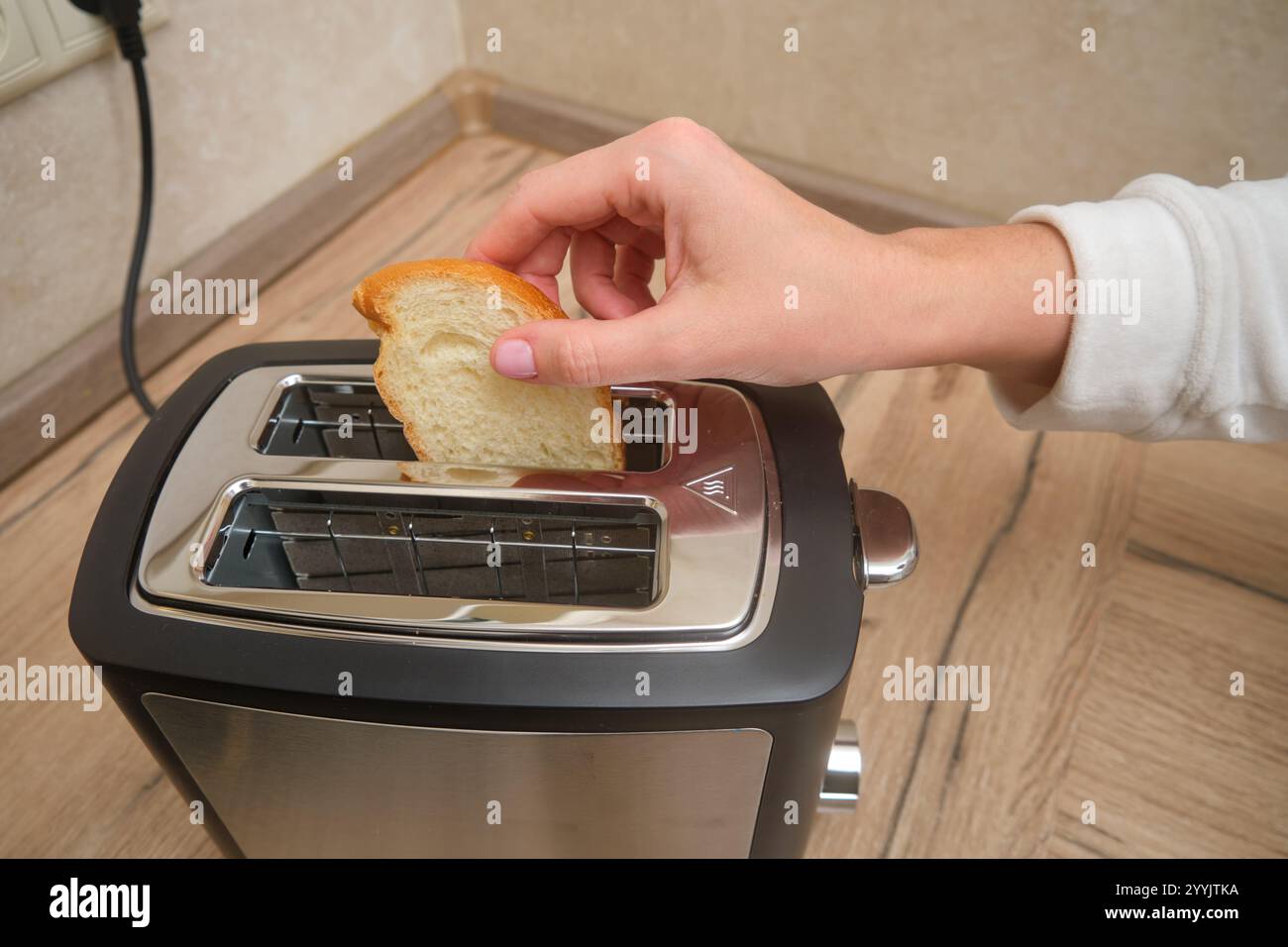 Hand placing slice of bread into a stainless steel toaster on a wooden ...