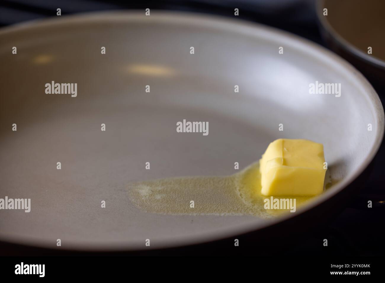 A pan with a piece of butter on it. The butter is melting and spreading ...