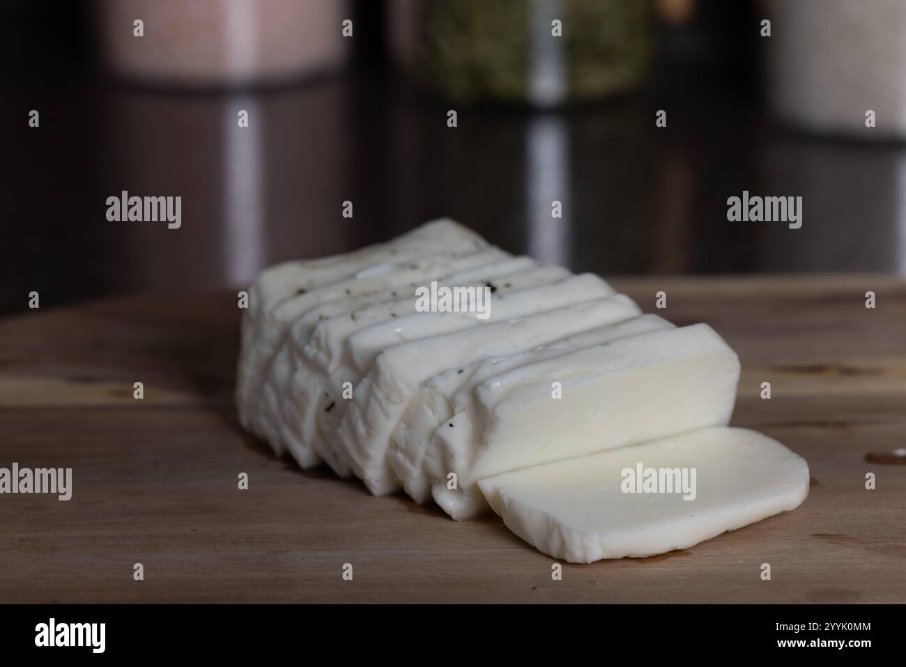 A block of halloumi cheese is sliced into pieces on a wooden cutting ...