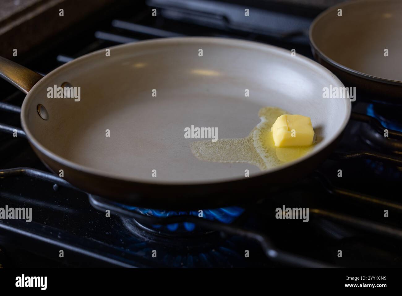 A pan with a piece of butter on it. The butter is melting and spreading ...