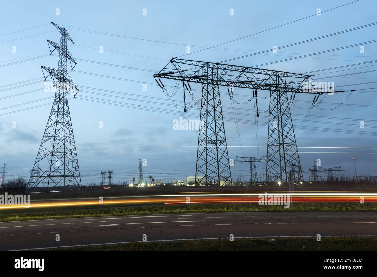 High-voltage pylons next to a road with light traces of passing cars ...