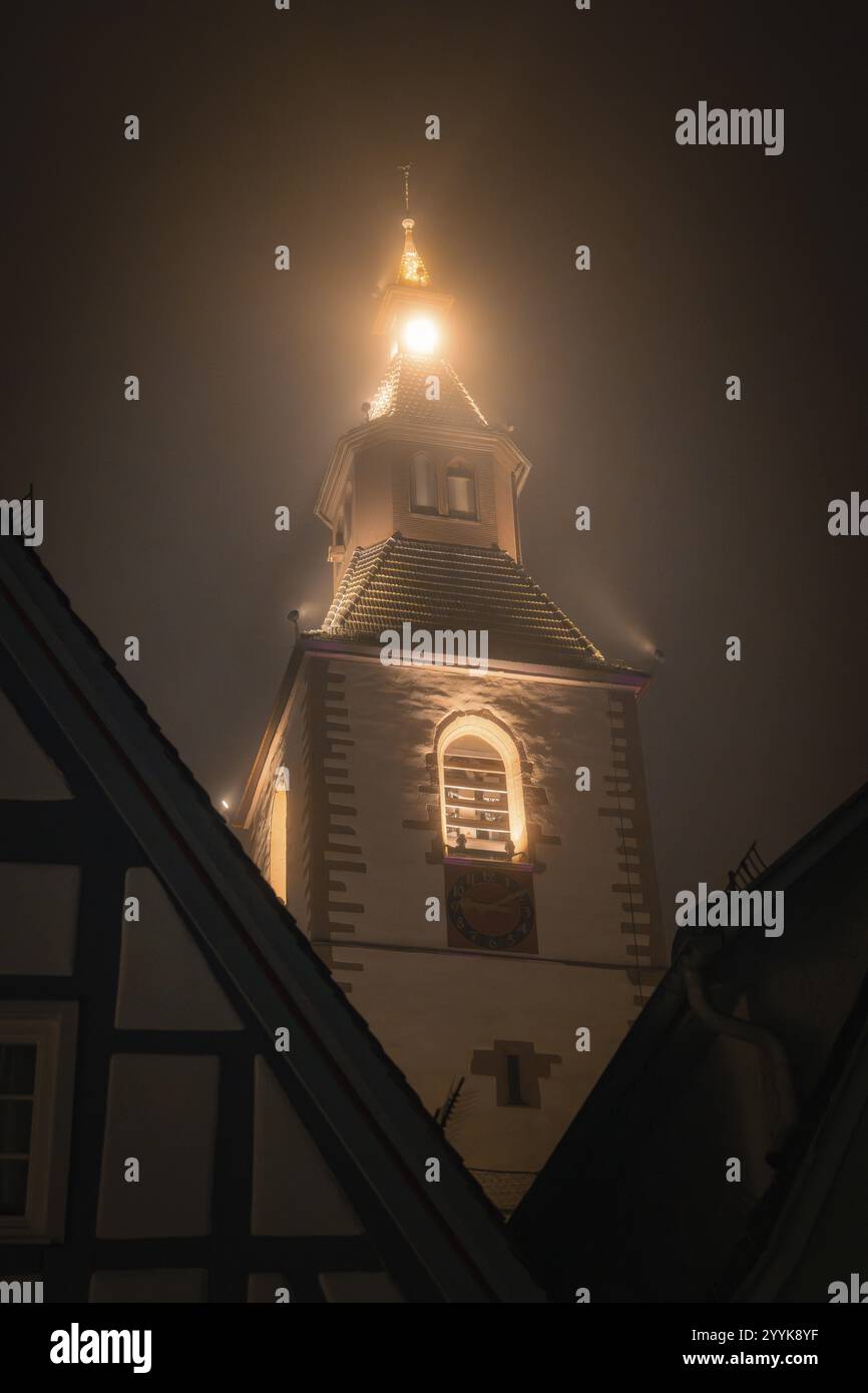 A church tower at night, shrouded in thick fog and illuminated by warm ...