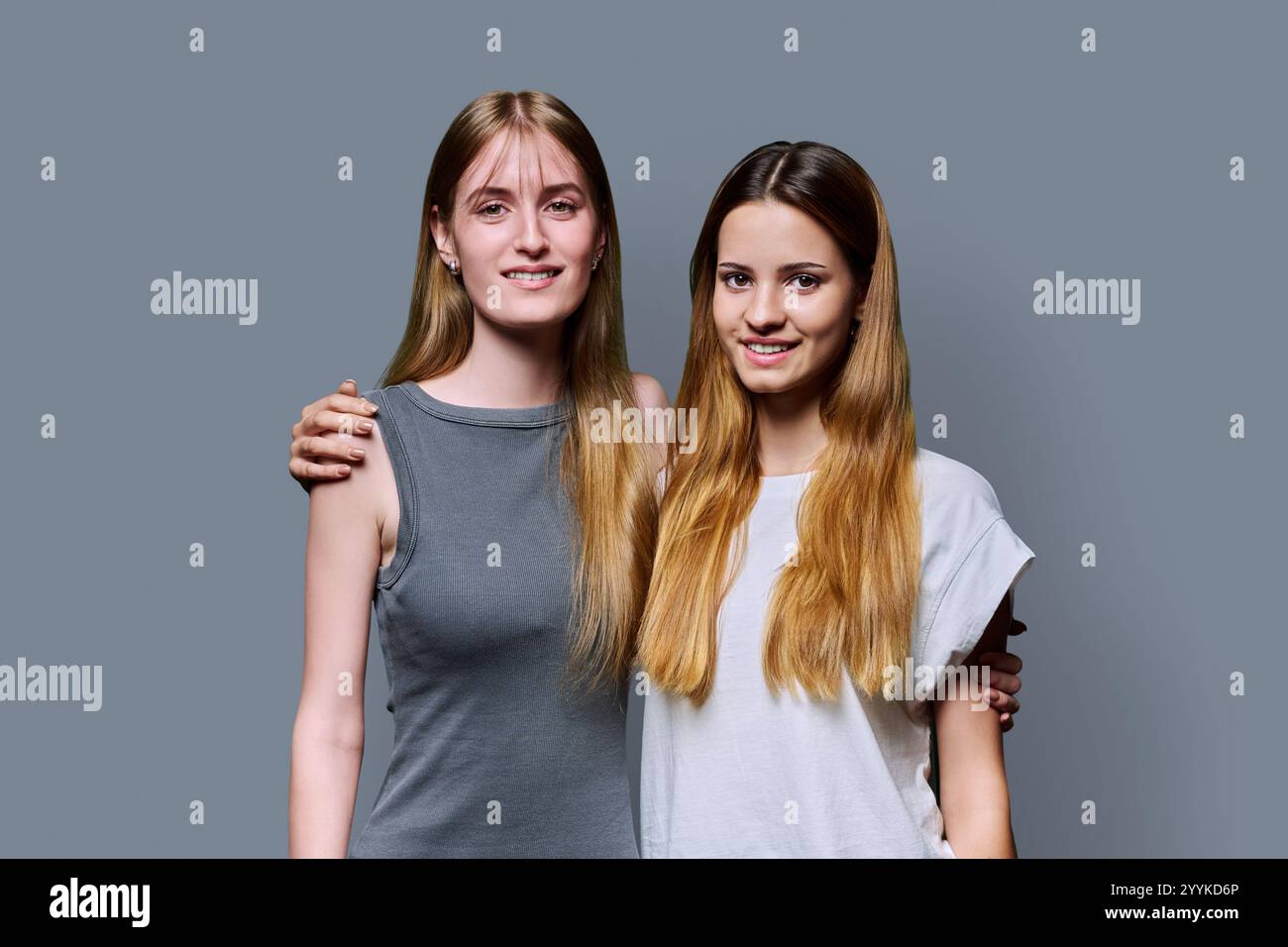 Two smiling hugging girlfriends, teenage girls posing on gray studio ...
