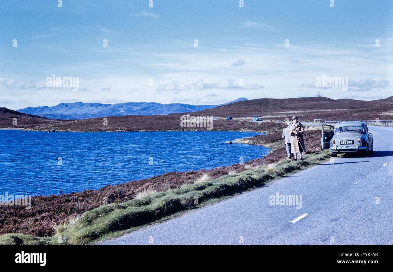 Historical photo of people by a loch or lake and an old Rover car ...