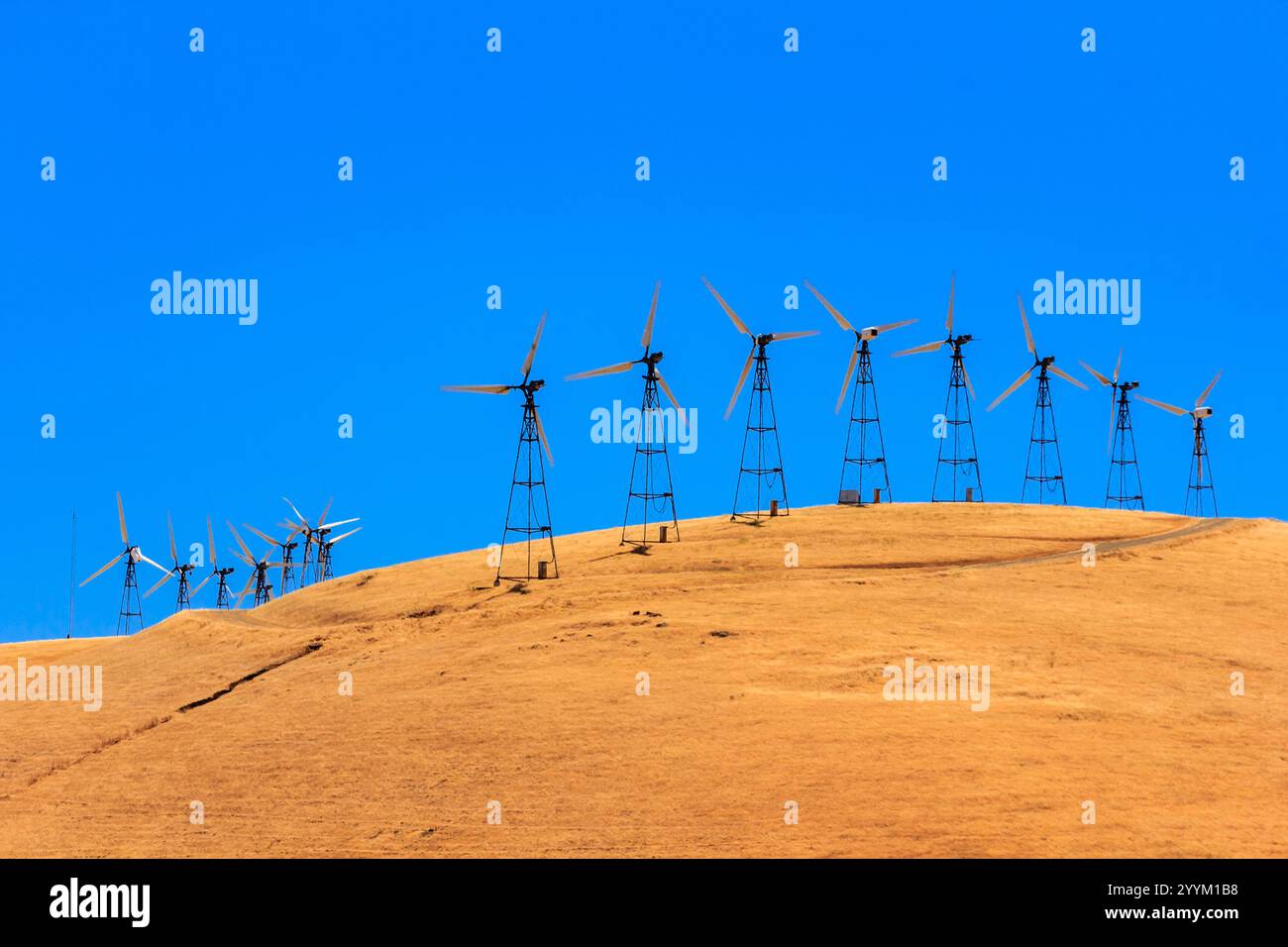 A row of windmills are on a hillside. The windmills are tall and spread ...