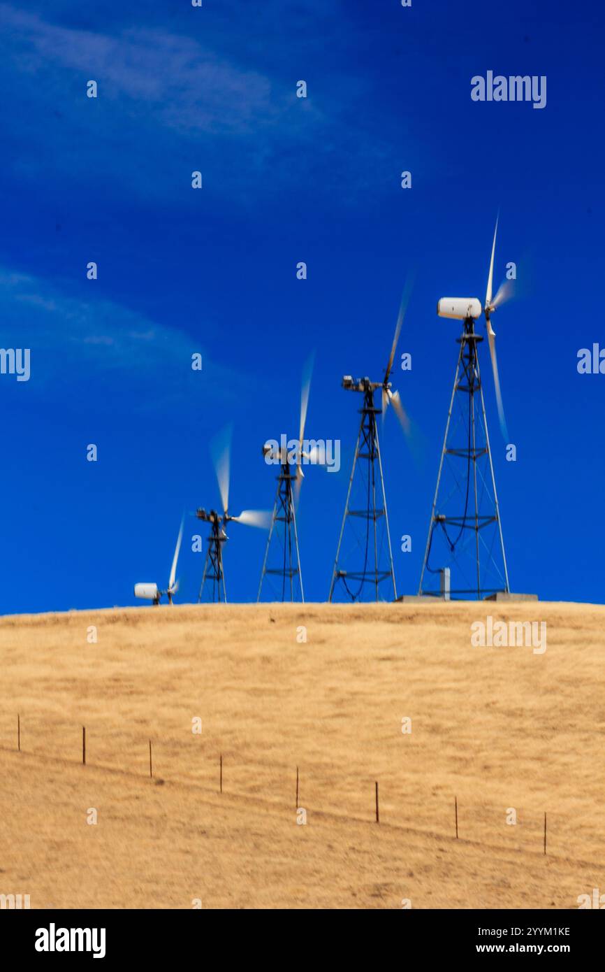 A cluster of wind turbines are standing on a hill, with the sun shining ...
