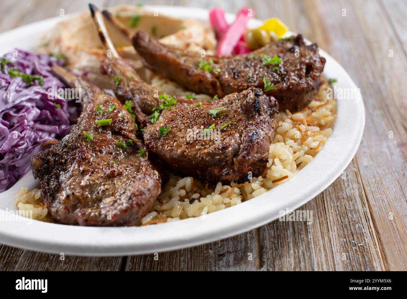 A view of a plate of lamb chops, featuring rice pilaf, cabbage salad ...