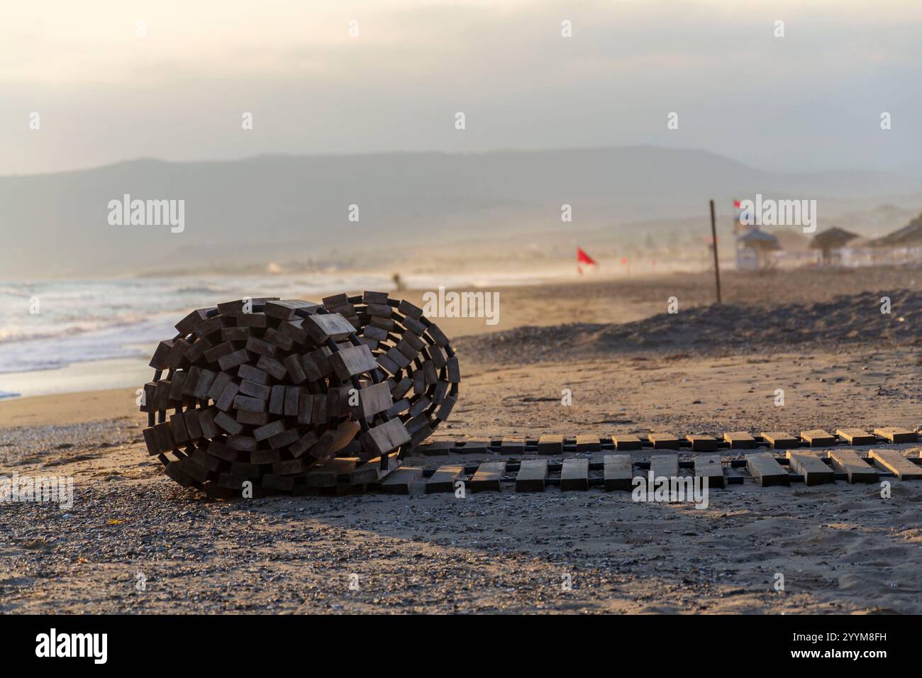Outdoor roll out wooden beach pathway on the seashore, red flags in ...