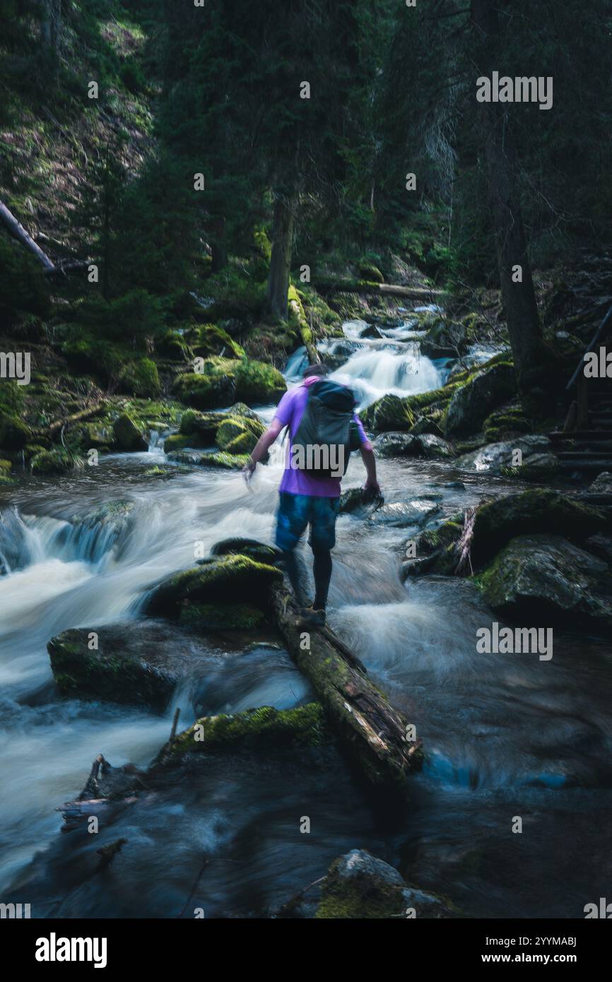 A man carrying a backpack carefully crosses a river using a sturdy log ...