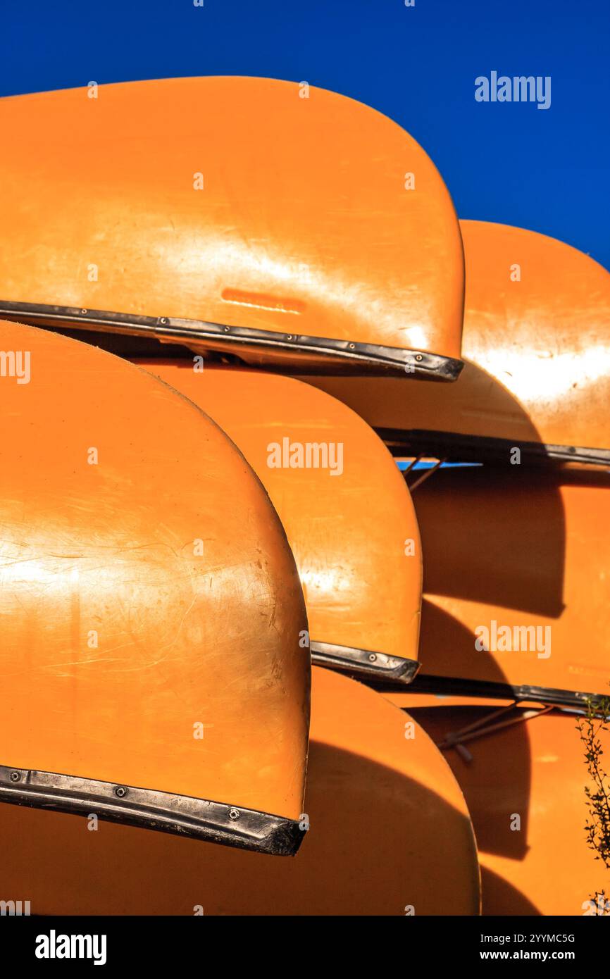 A row of orange canoes are stacked on top of each other. The canoes are ...