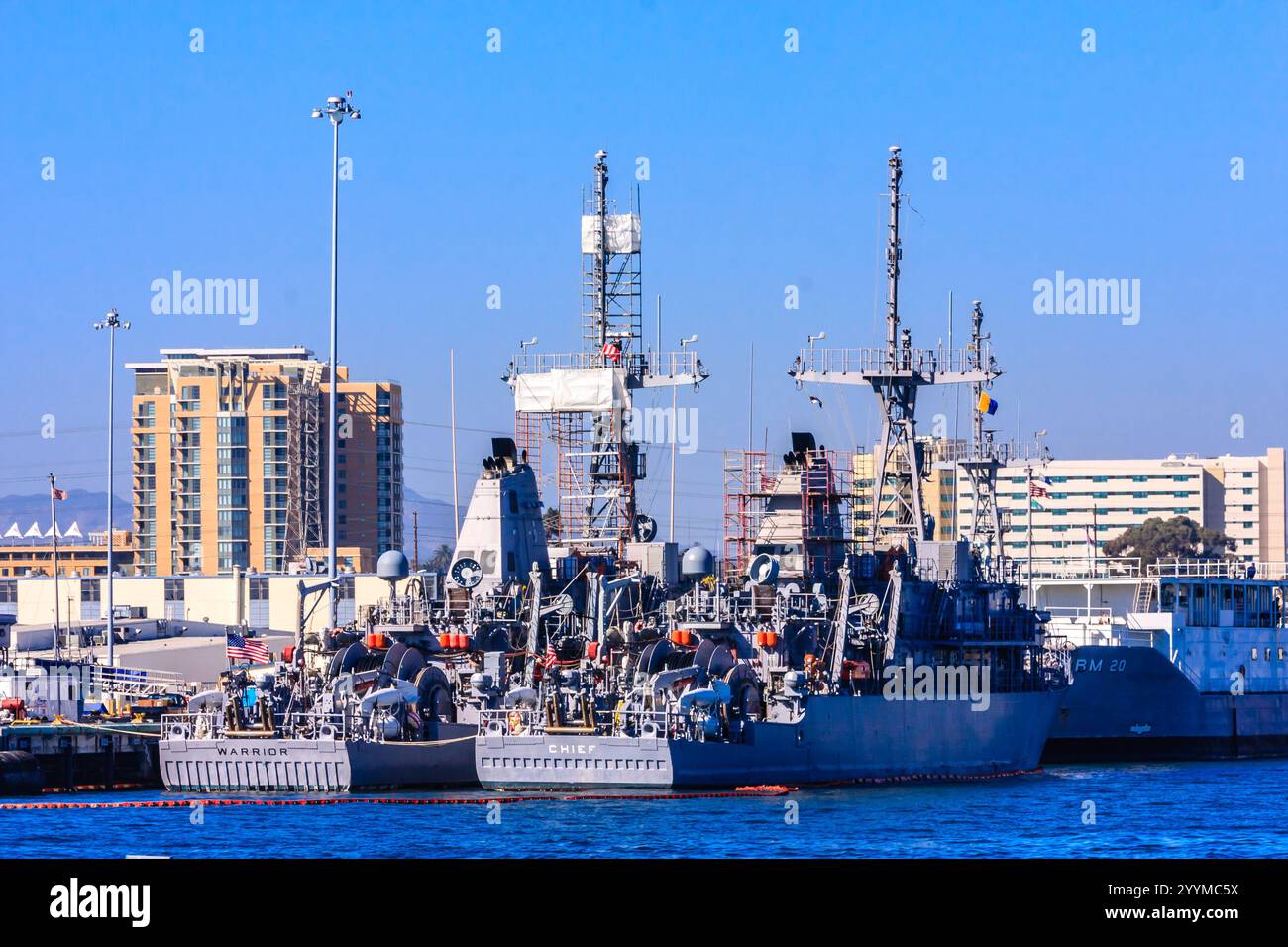 Two large navy ships are docked at a pier. The ships are surrounded by ...