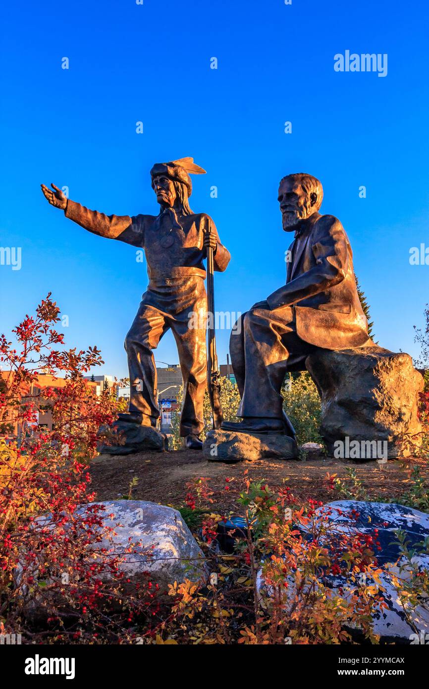 Two statues of men, one of them holding a walking stick, are sitting on ...