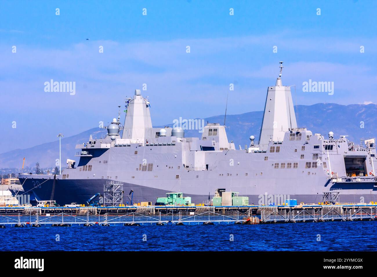 A large navy ship is docked at a pier. The sky is clear and the water ...