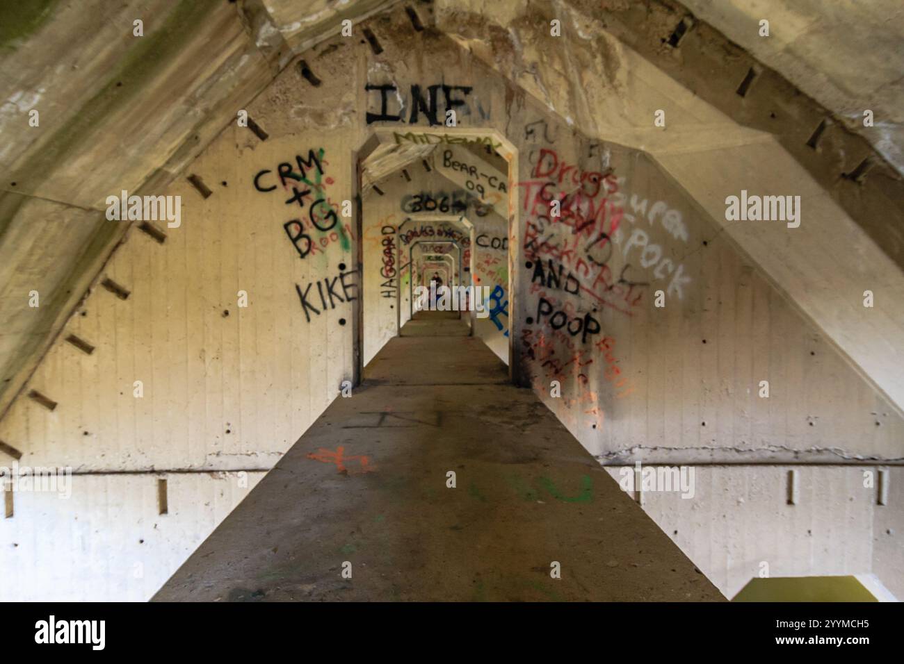 A long, narrow tunnel with graffiti on the walls. The graffiti includes ...