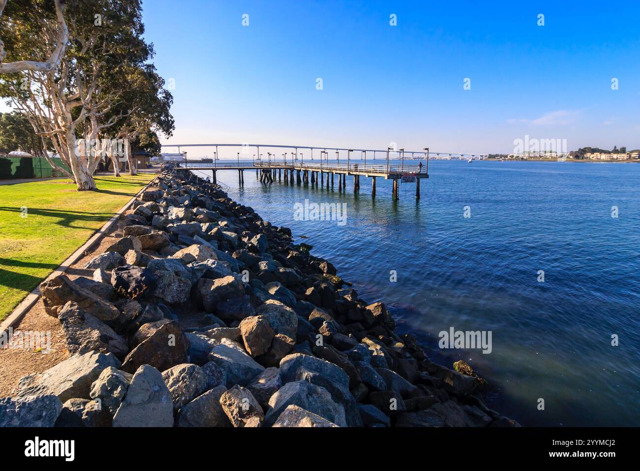 A rocky shoreline with a pier and a dock. The water is calm and the sky ...