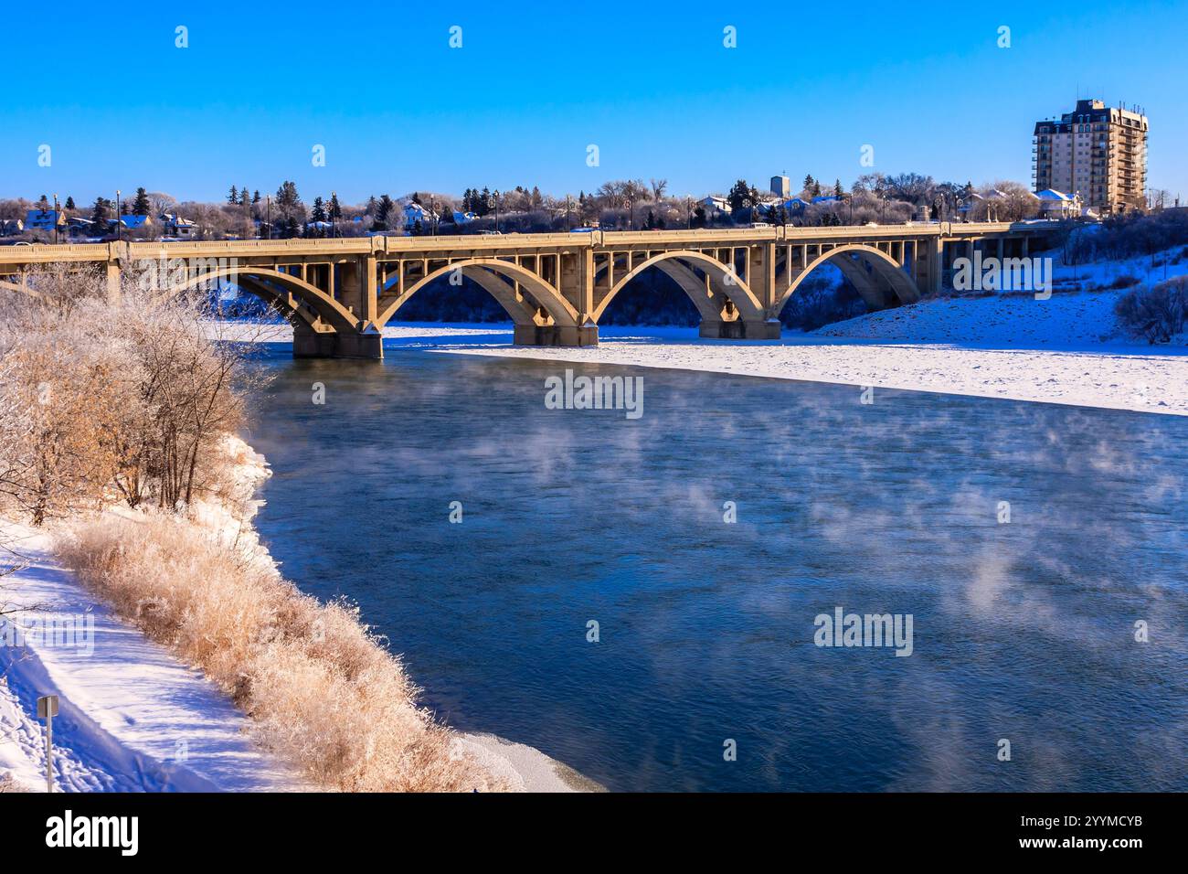 A bridge spans a river with a snowy bank on either side. The bridge is ...