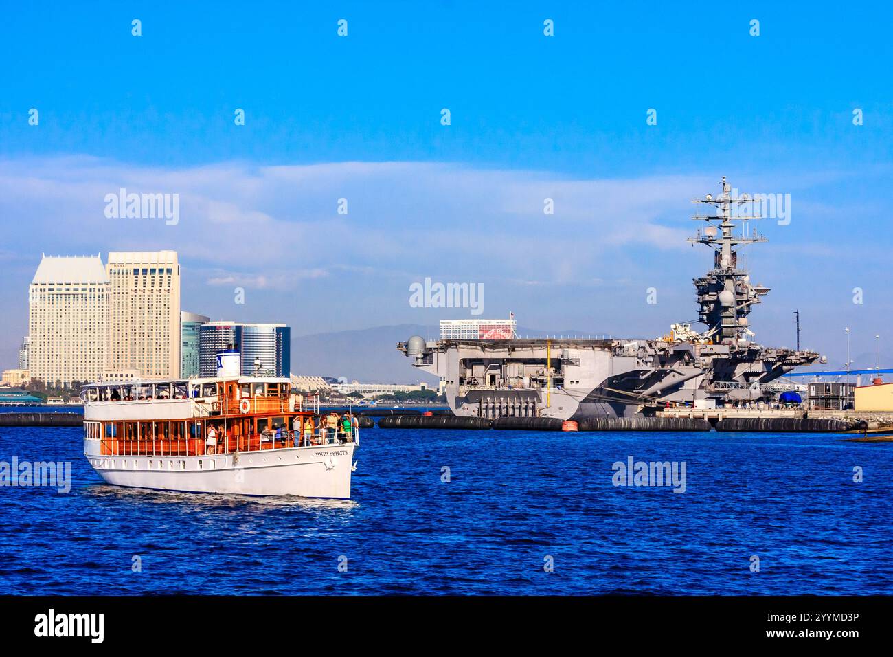 A large Navy ship is sailing in the ocean near a city. The ship is a ...