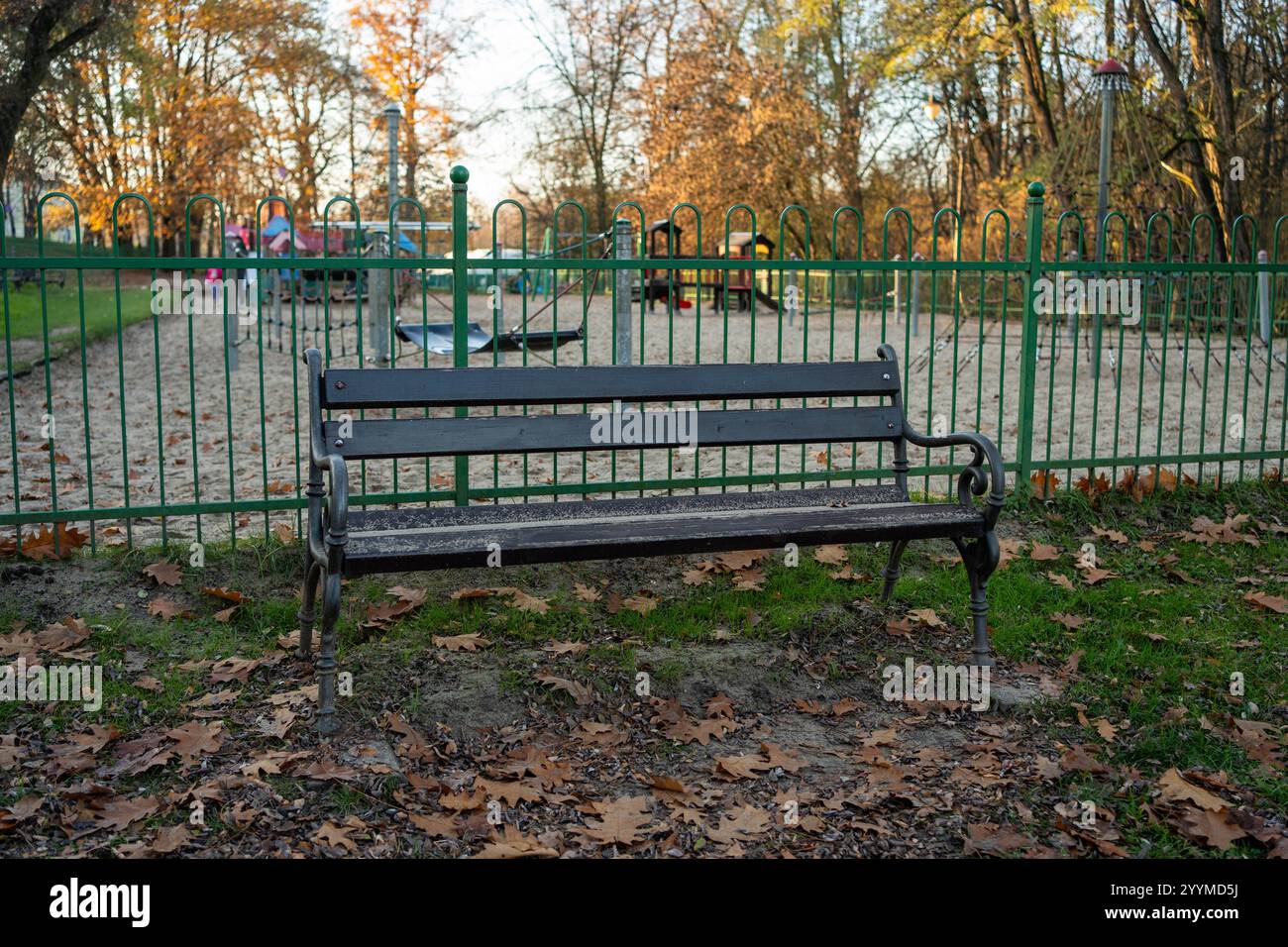 An empty playground surrounded by green fencing in a park during autumn ...