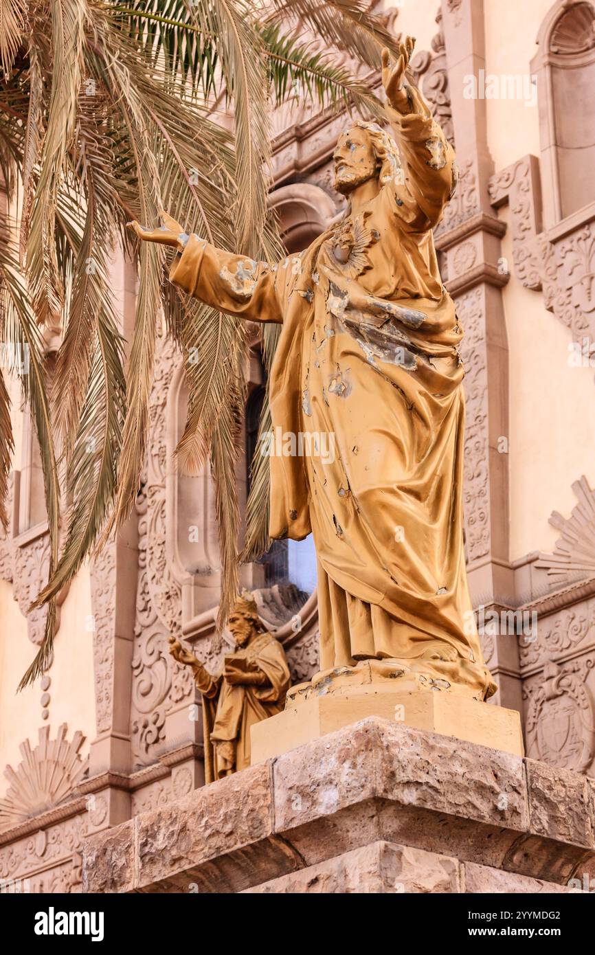 A statue of Jesus is on a pedestal in front of a building. The statue ...