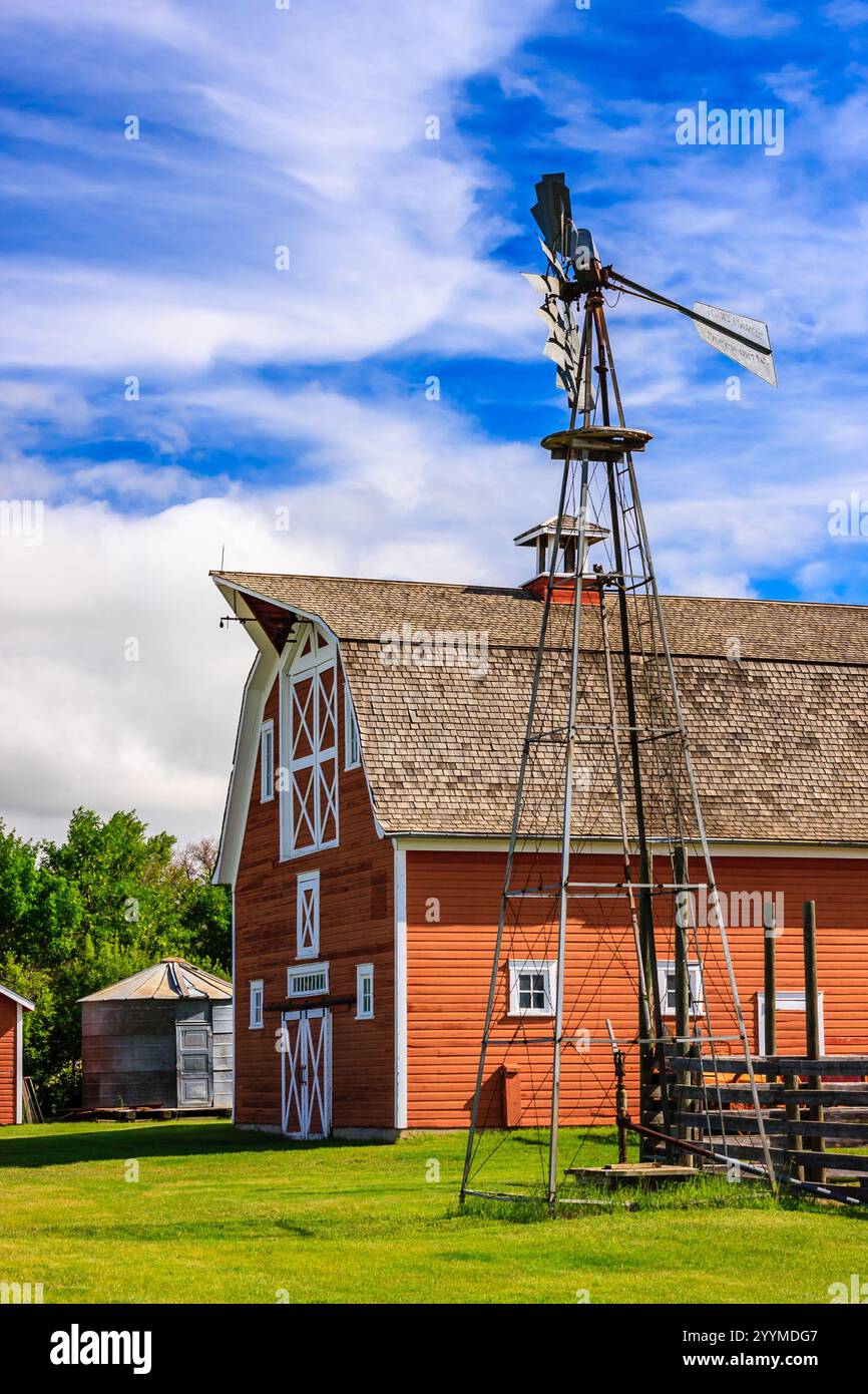 A windmill is on the roof of a red barn. The barn is surrounded by a ...