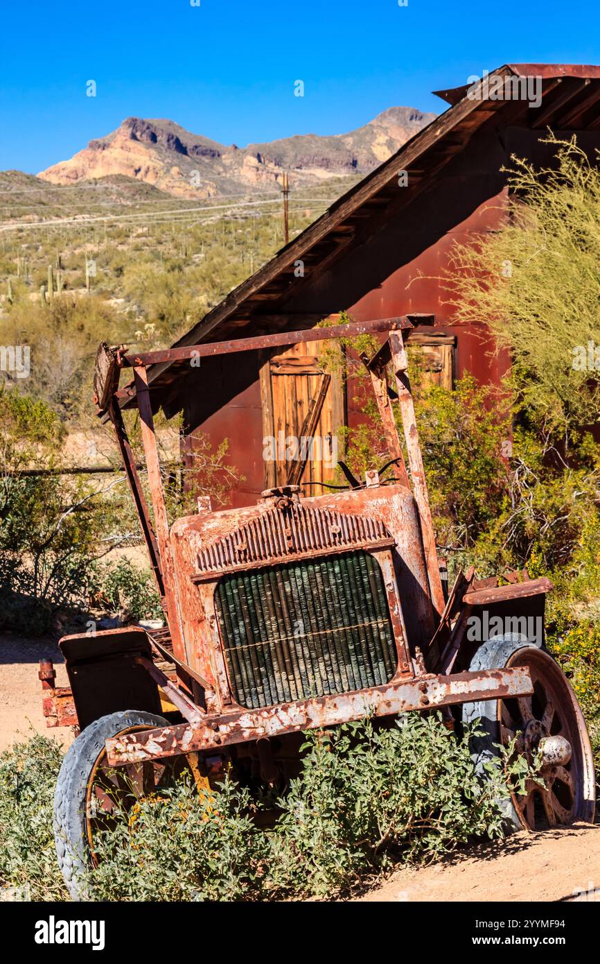 An old, rusted car is sitting in front of a red house. The car is ...