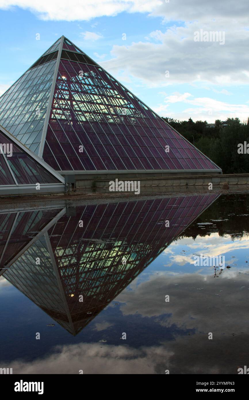 A large glass pyramid building with a large pool of water reflecting it ...
