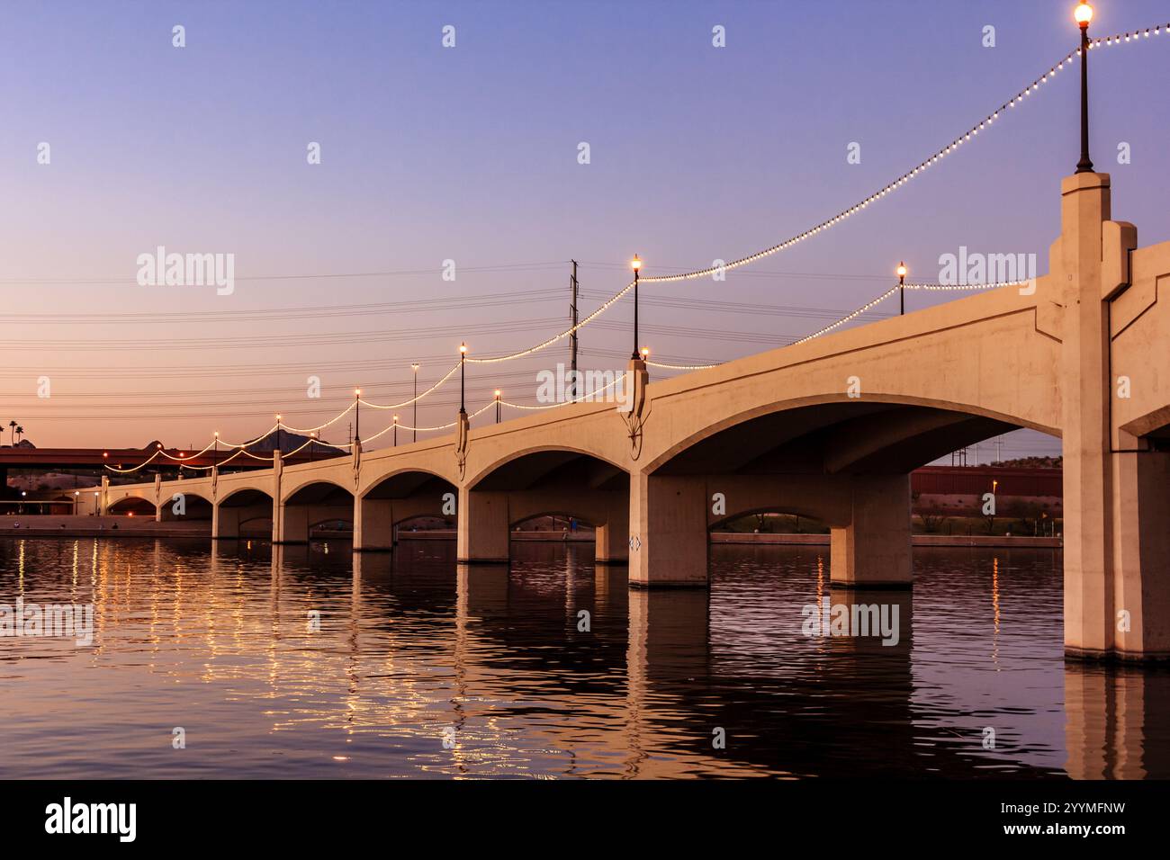 A bridge with lights hanging from it over a body of water. The lights ...