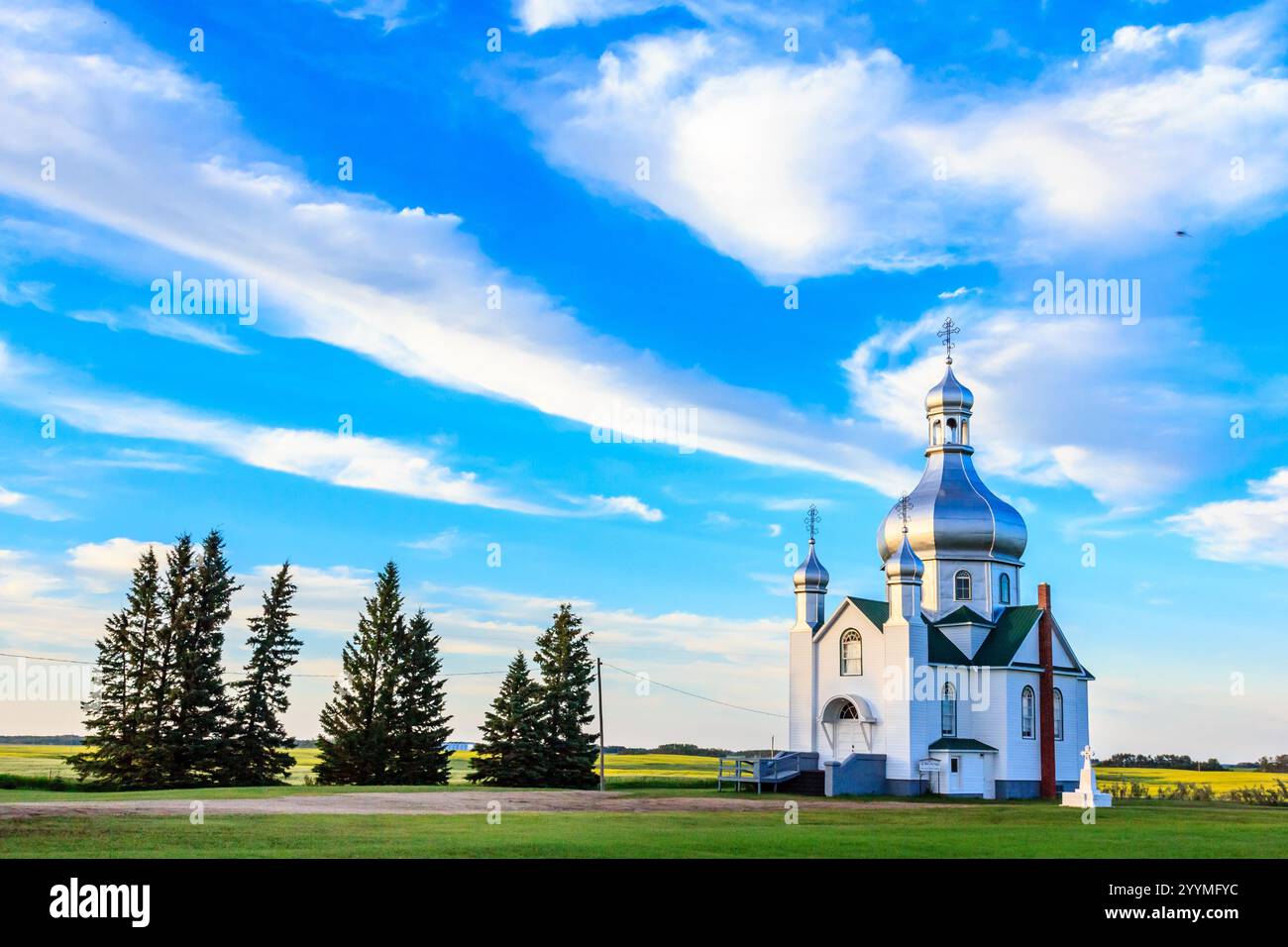 A white church with a steeple sits in a field with a blue sky. The ...