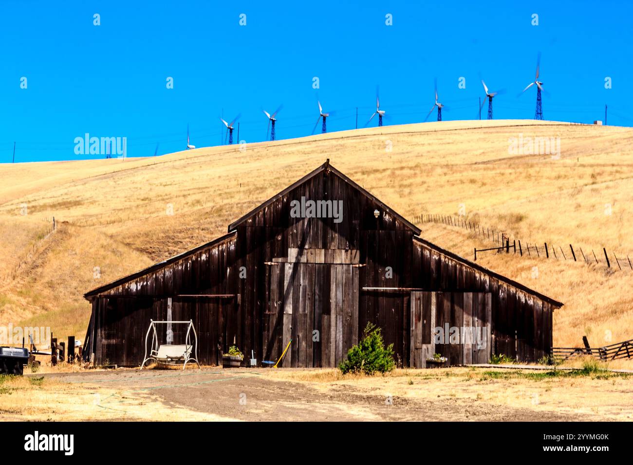 A large, old barn sits on a hillside with a field of wind turbines in ...