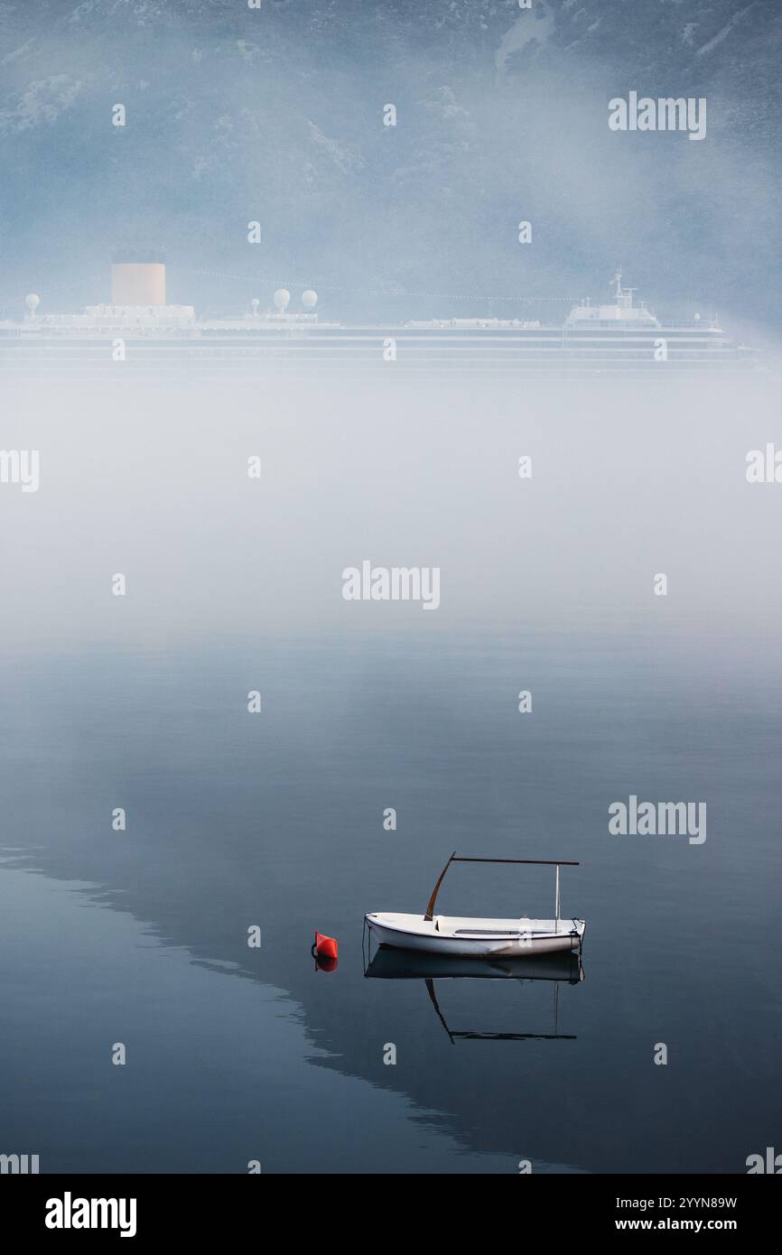 Small white boat with red buoy floating on calm water with a large ...