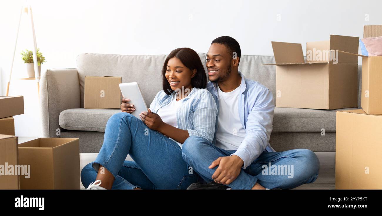 Relocation concept. Happy black couple using tablet, searching new ...