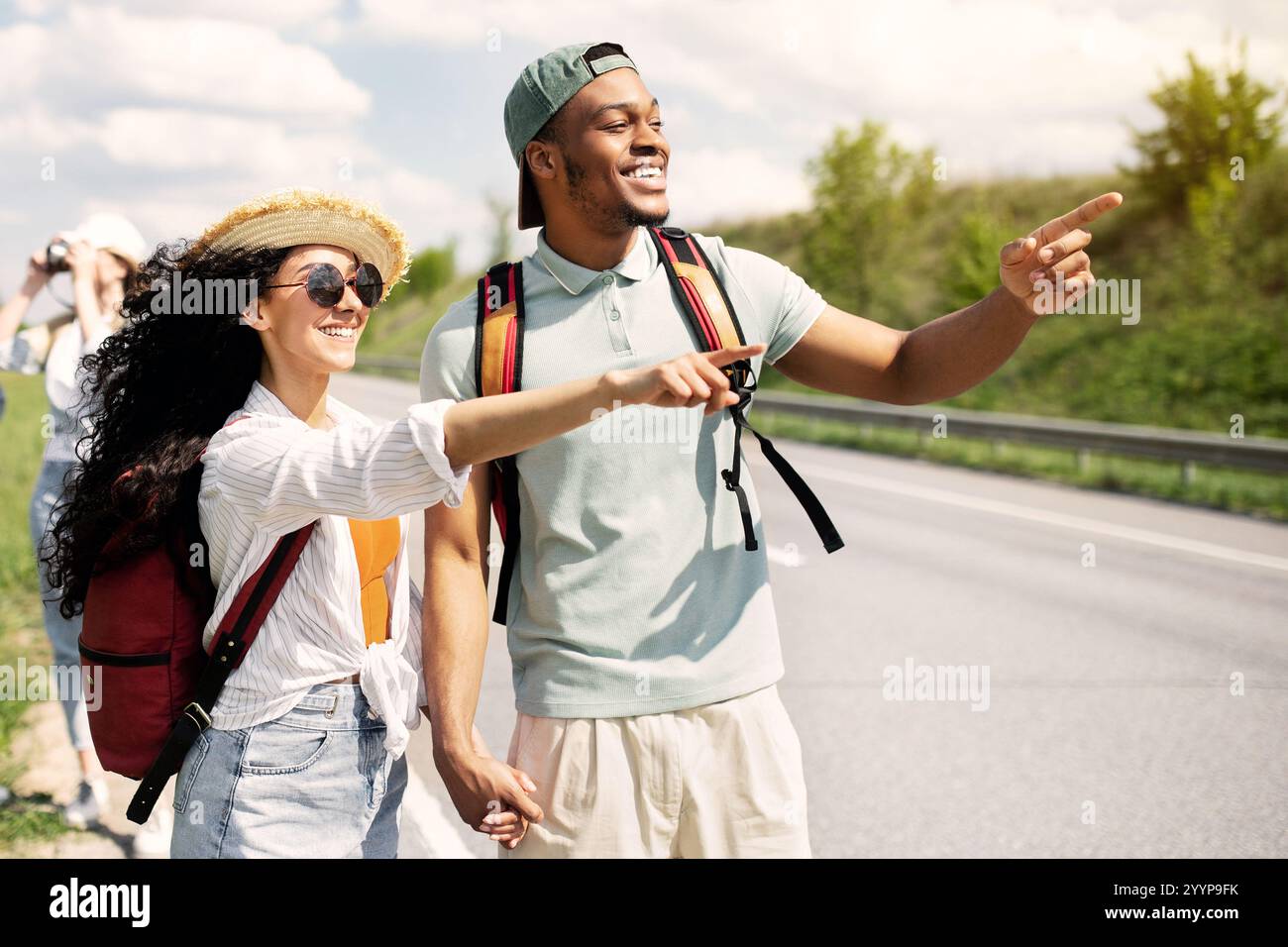 Millennial travelers with backpacks walking along road, hitchhiking in ...