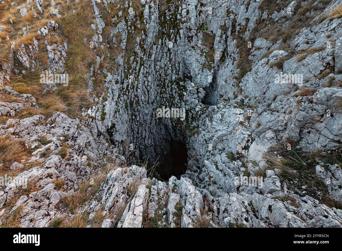 Impressive vertical cave entrance surrounded by rocks and dry grass in ...