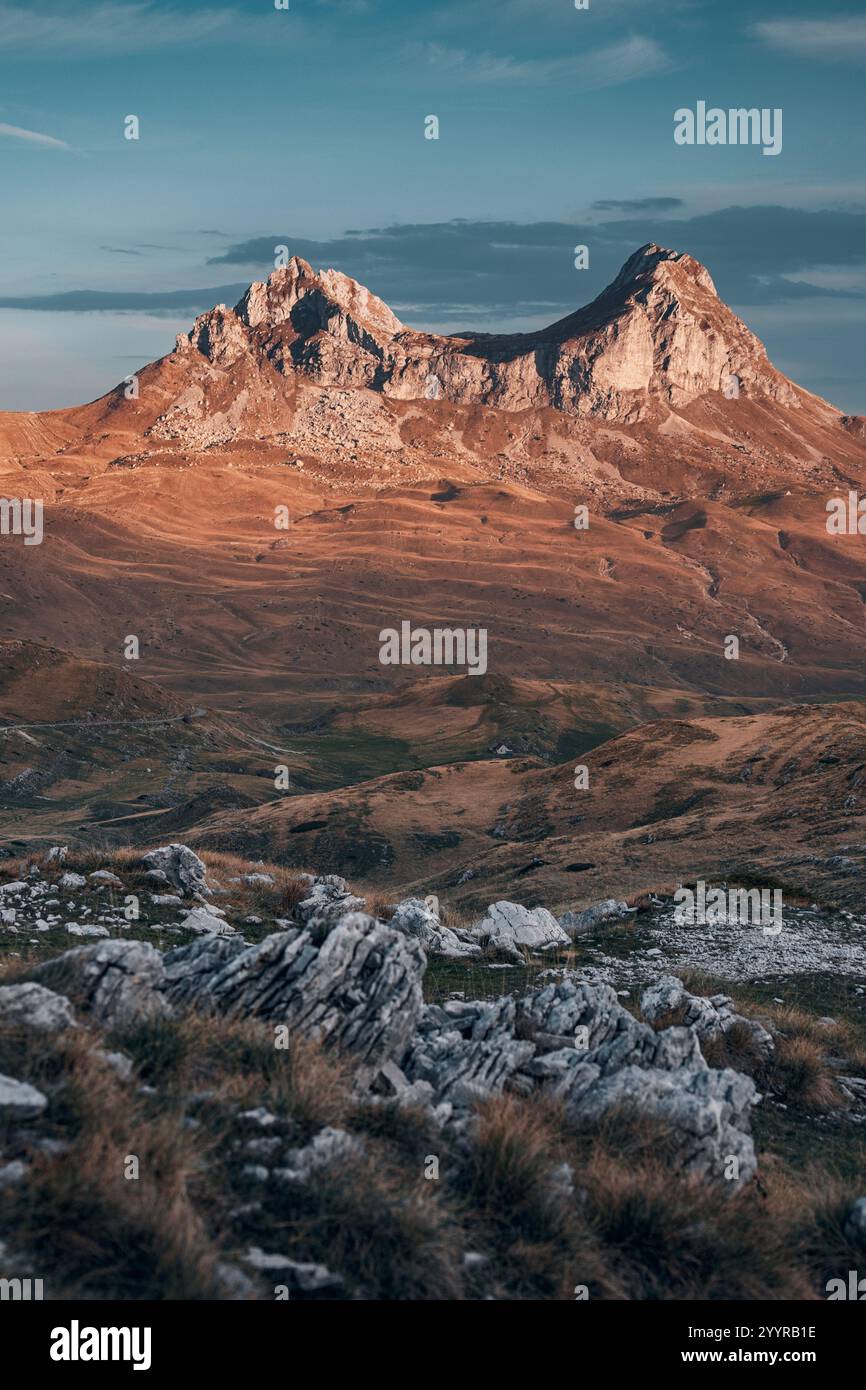 Warm sunlight illuminating rocky terrain and majestic mountain peaks in ...